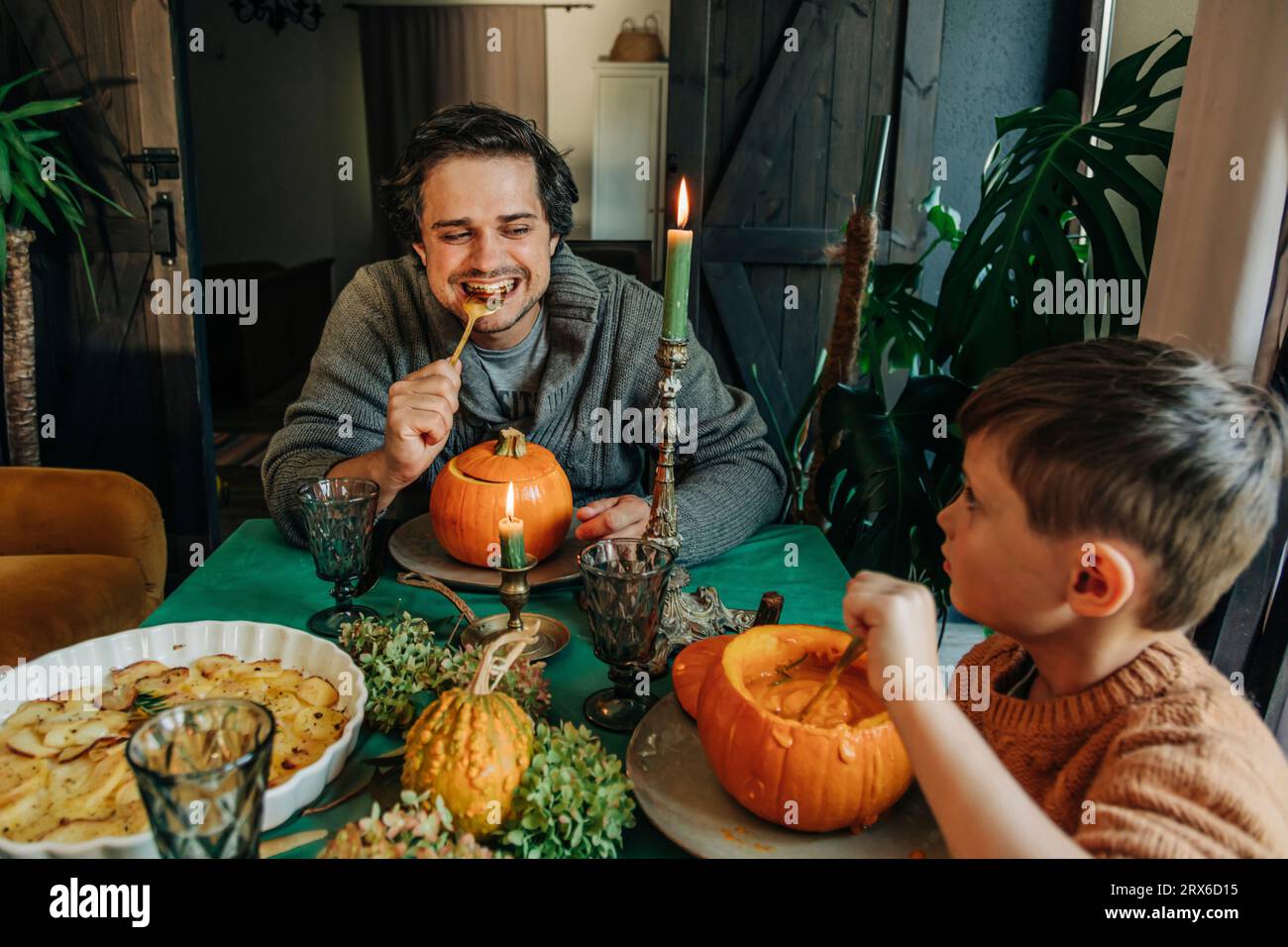 Playful father biting spoon with son sitting at dining table Stock ...
