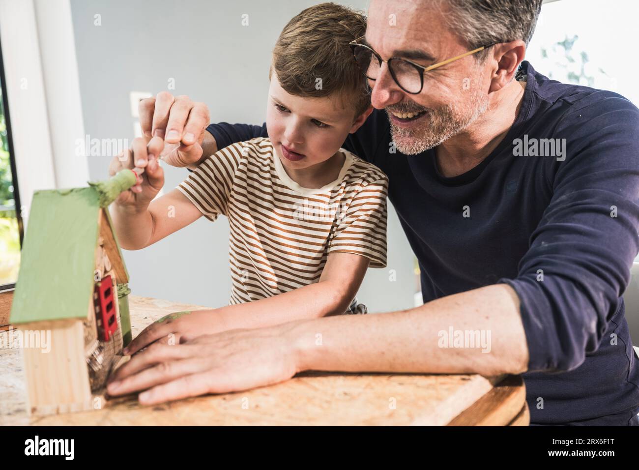 Smiling grandfather teaching grandson to paint model house at home ...