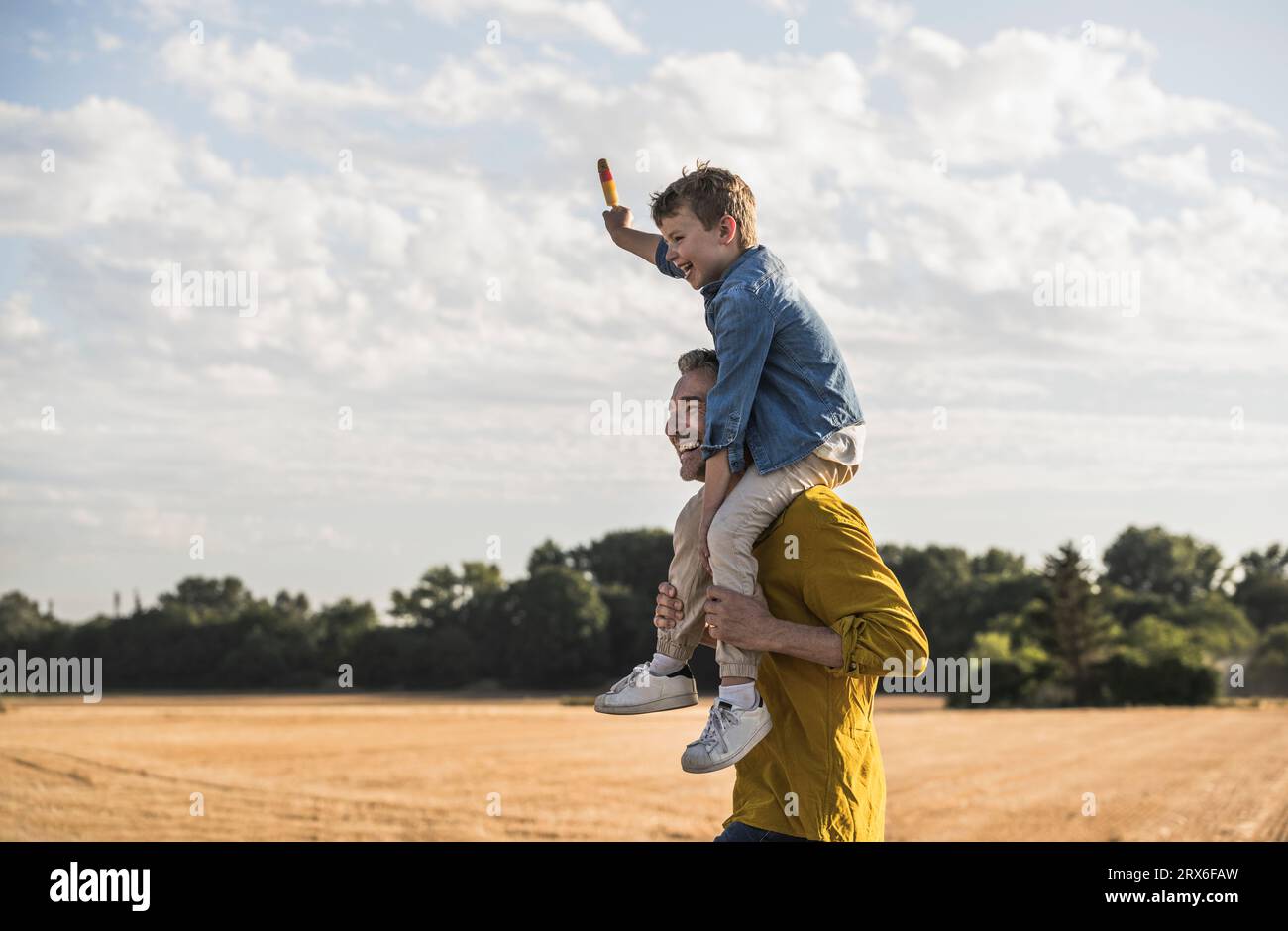 Happy boy sitting on shoulders of grandfather at sunny day Stock Photo ...