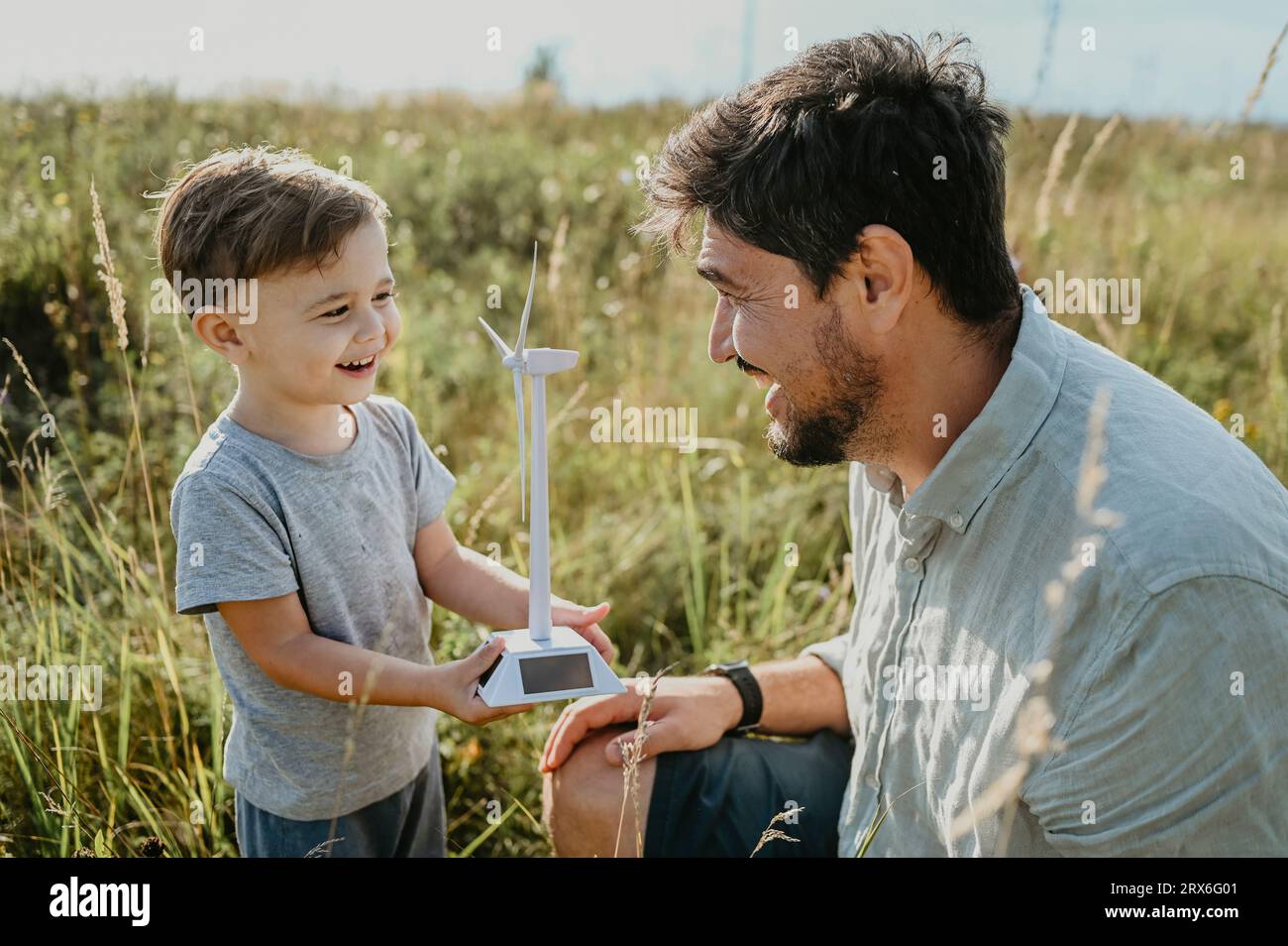 Smiling son showing wind turbine model to father in field Stock Photo ...