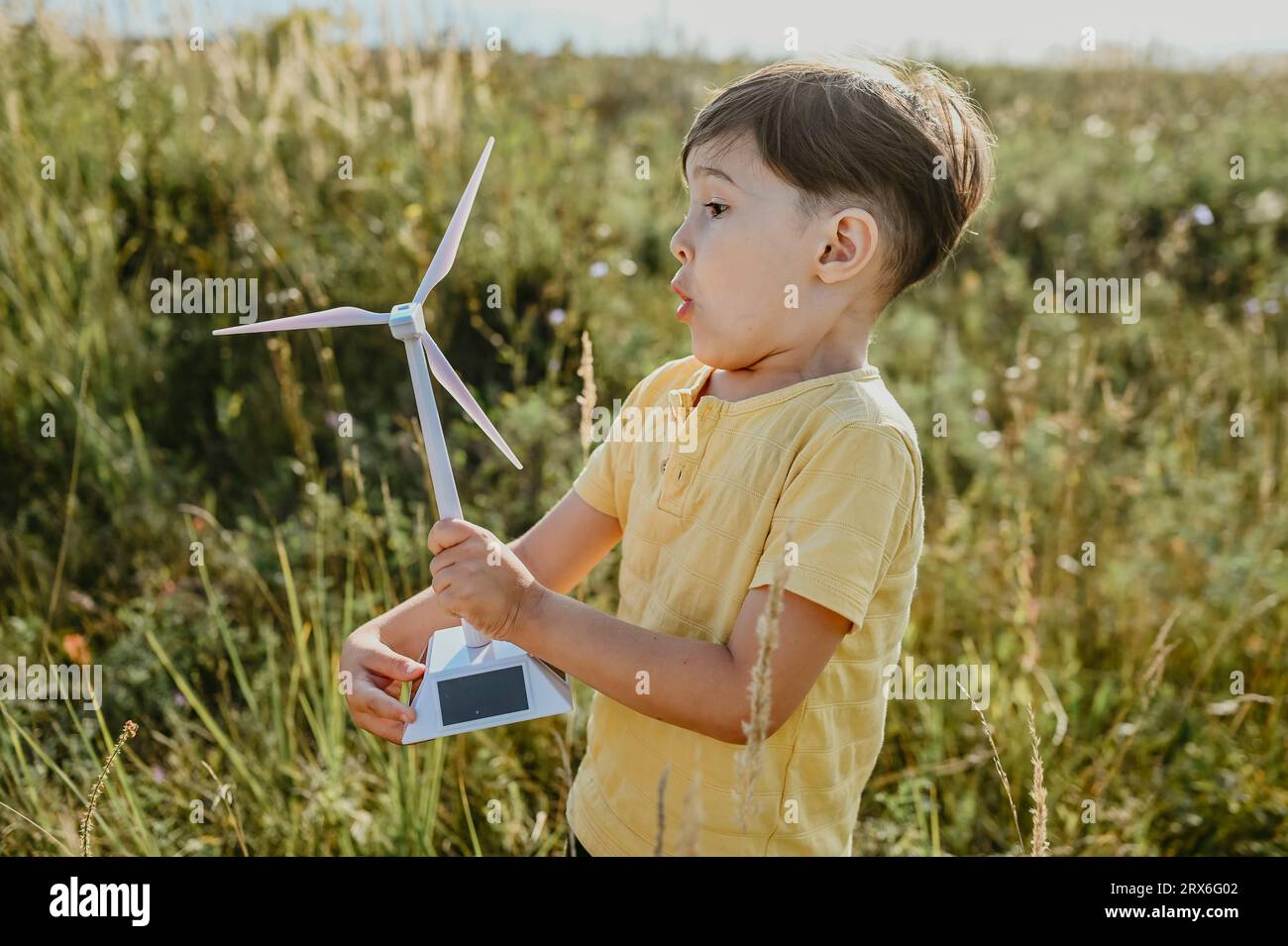 Boy blowing on wind turbine model in field Stock Photo - Alamy