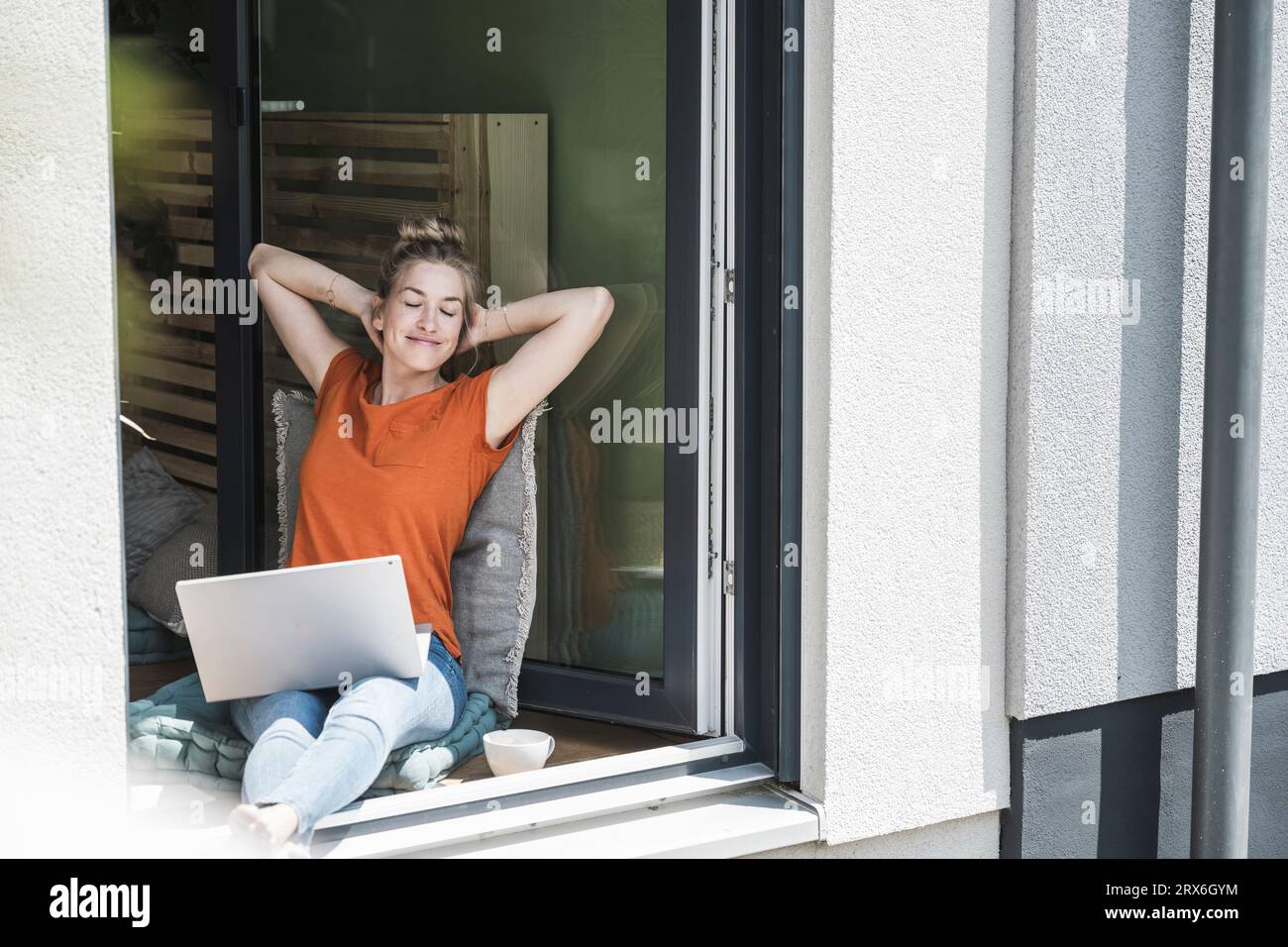 Woman relaxing by open window with laptop Stock Photo - Alamy