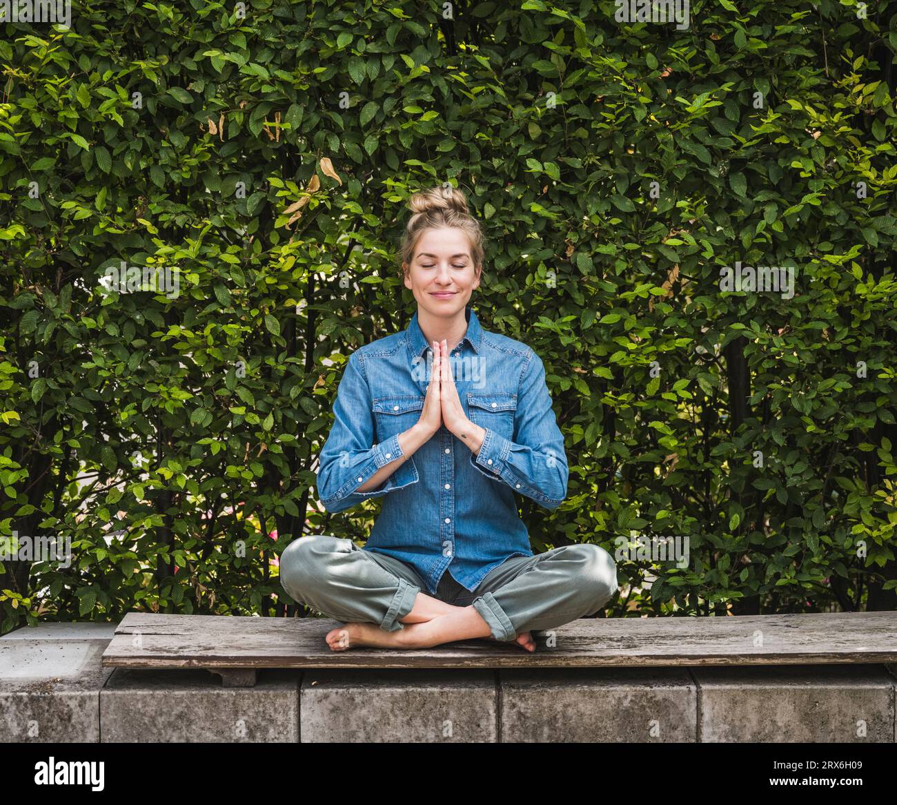 Portrait of woman meditating on bench in front of hedge Stock Photo - Alamy