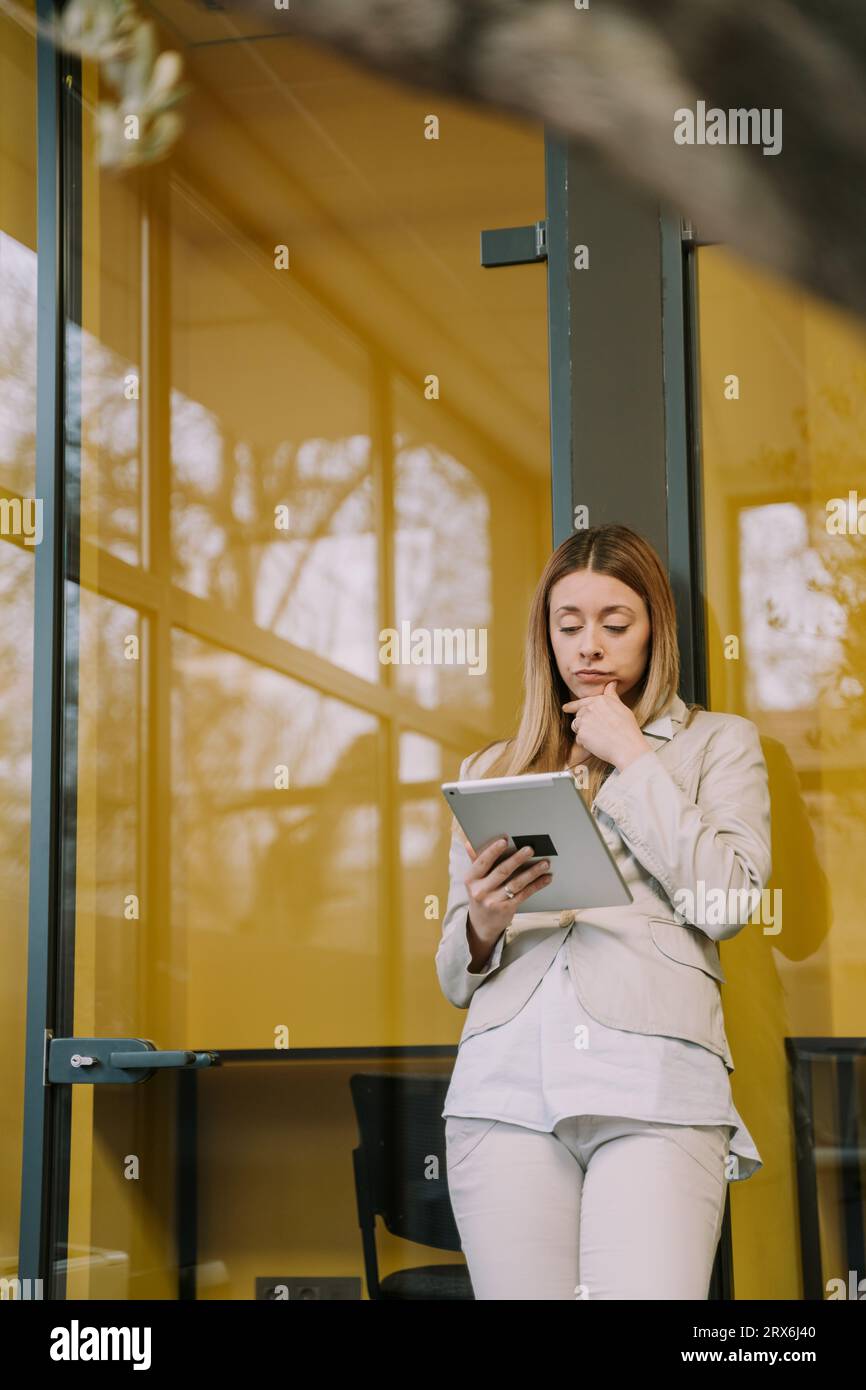 Beautiful blonde girl is checking something on her tablet and thinking ...