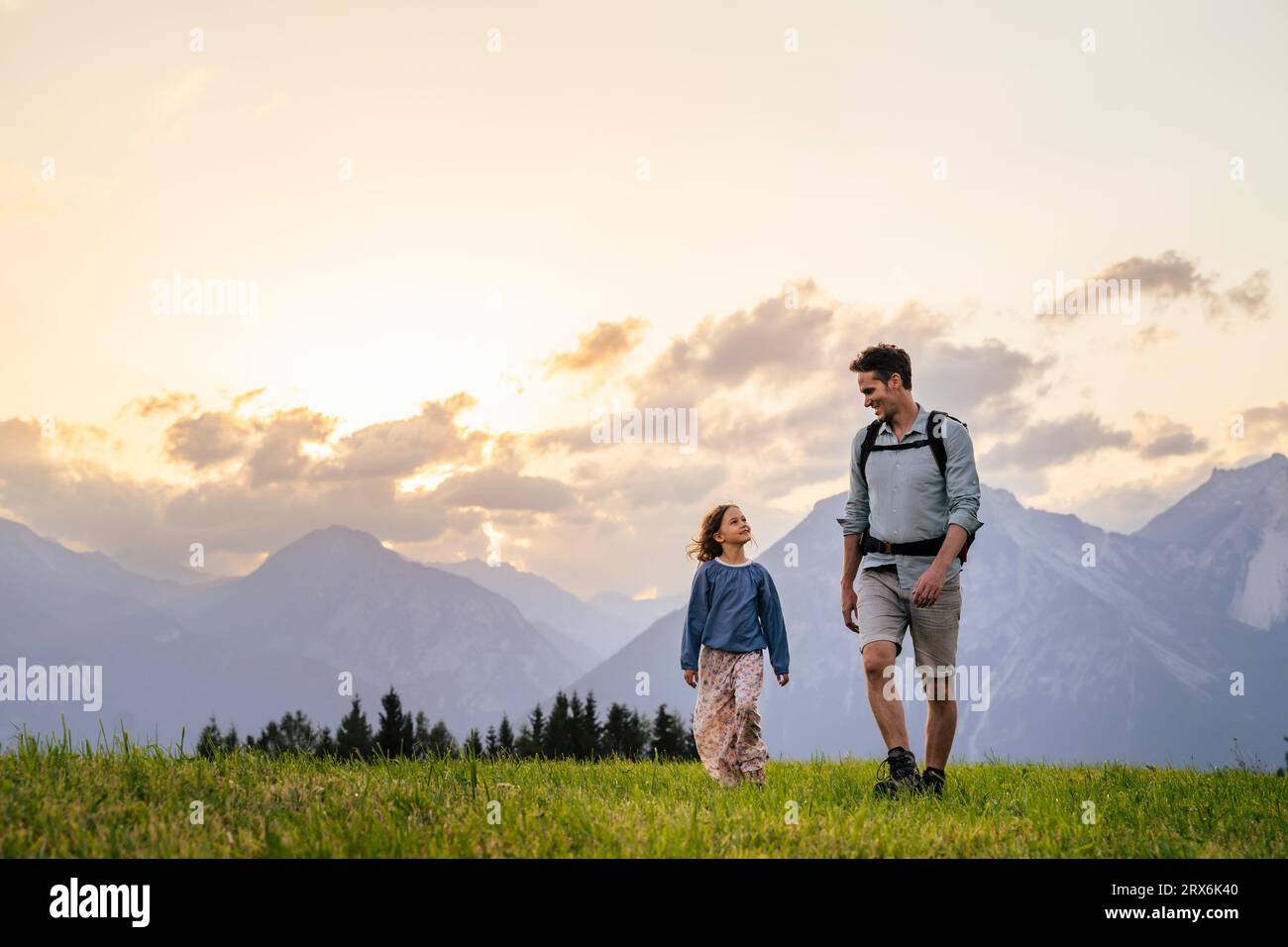 Father and daughter walking on grass in front of mountain range at ...