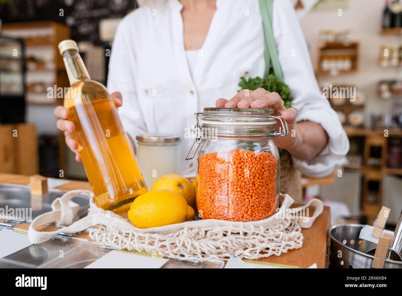 Woman putting glass cooking oil bottle in mesh bag at table Stock Photo ...