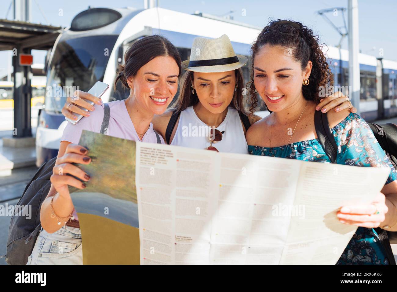 Happy friends together looking at map in front of train Stock Photo - Alamy