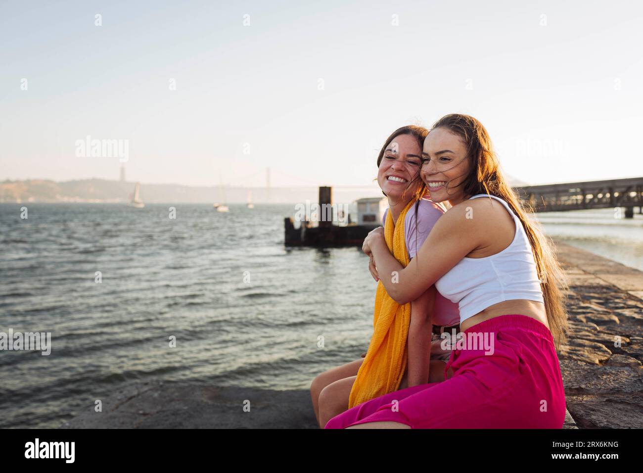 Happy woman hugging friend sitting on promenade Stock Photo - Alamy
