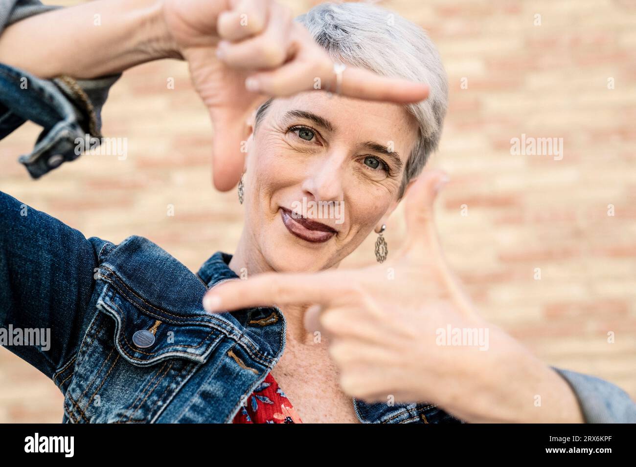 Smiling woman making finger frame sign in front of wall Stock Photo - Alamy