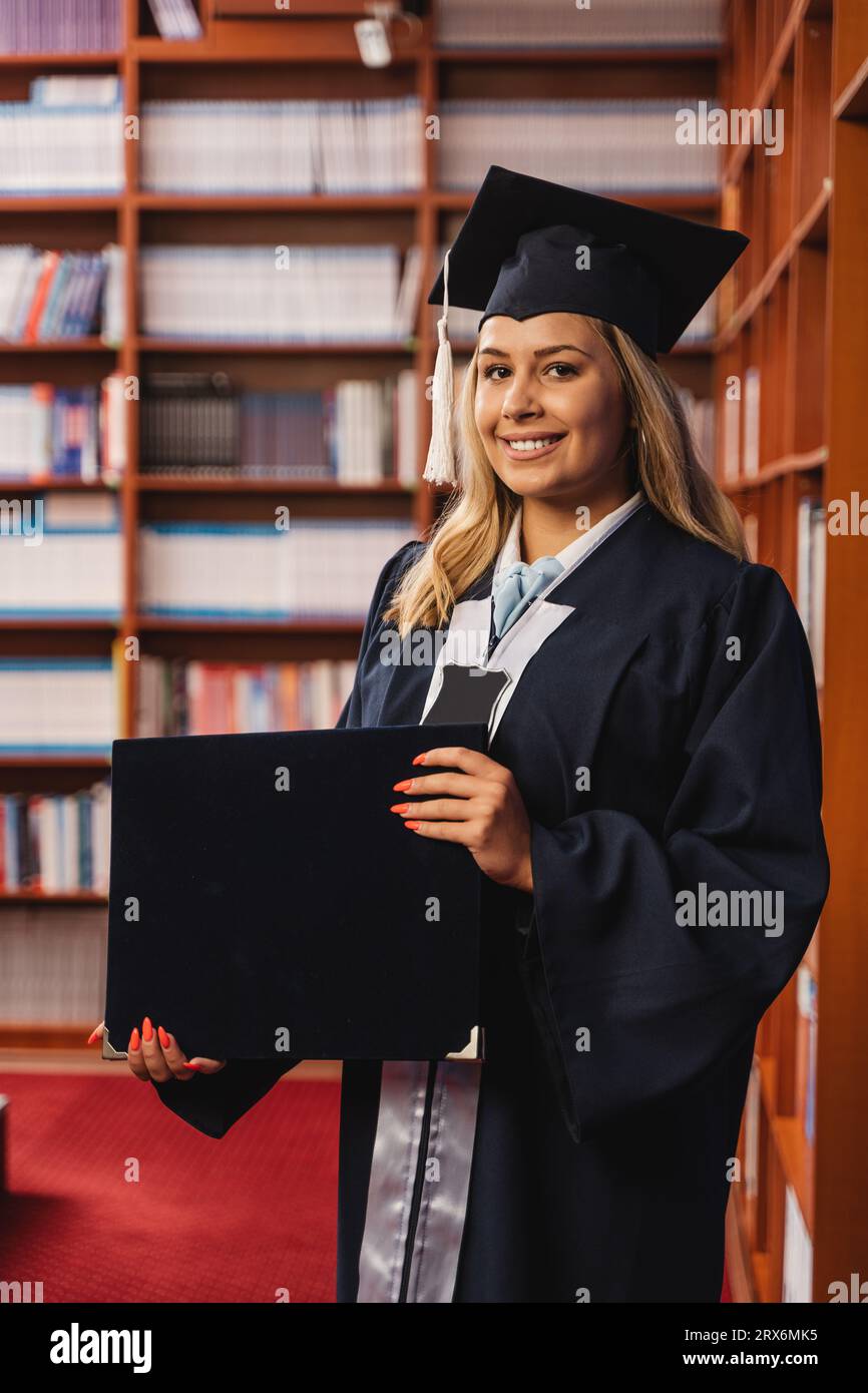 Young and happy graduate wearing a cap and gown and holding her ...