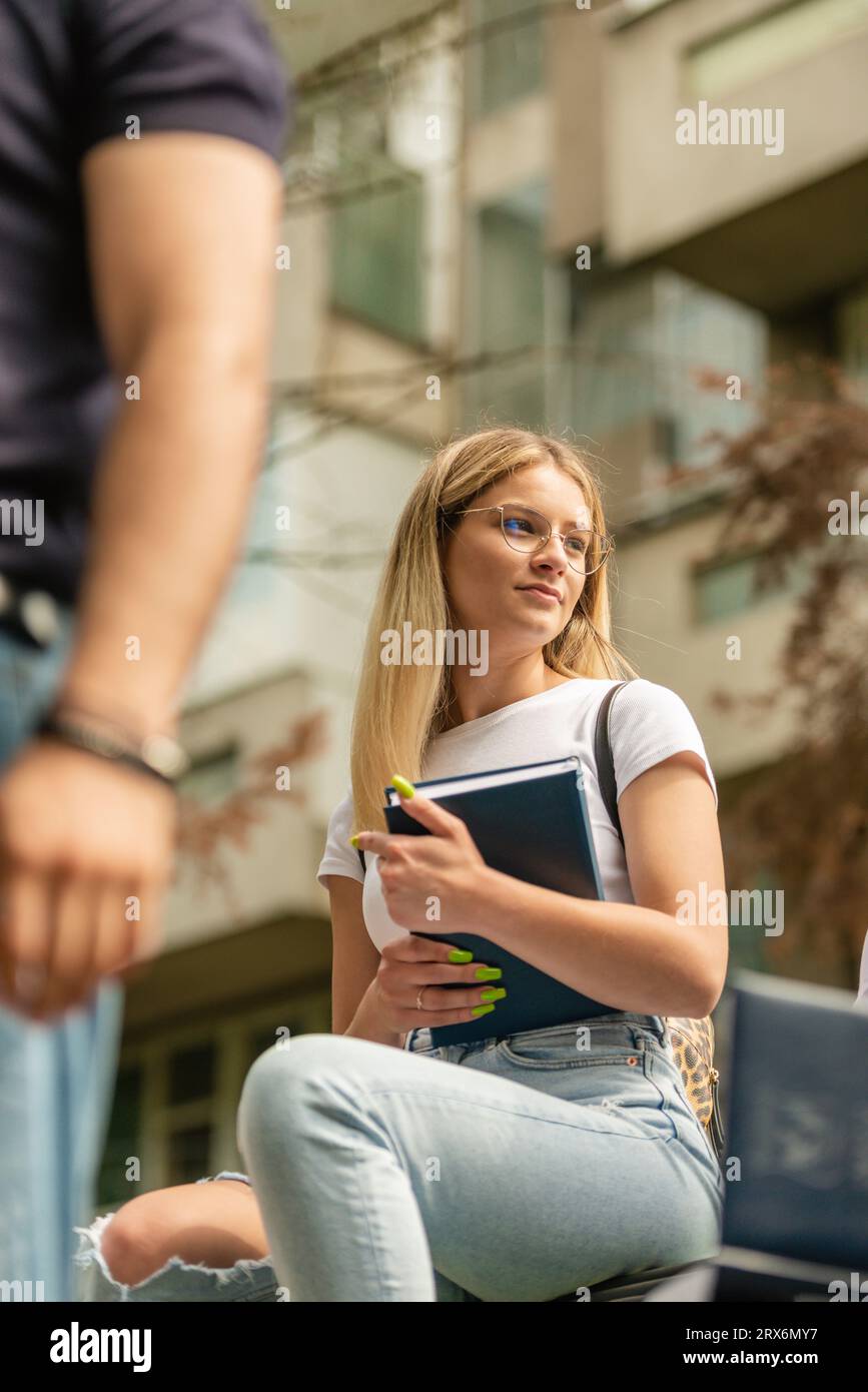 Portrait of young and beautiful female student sitting down outside ...