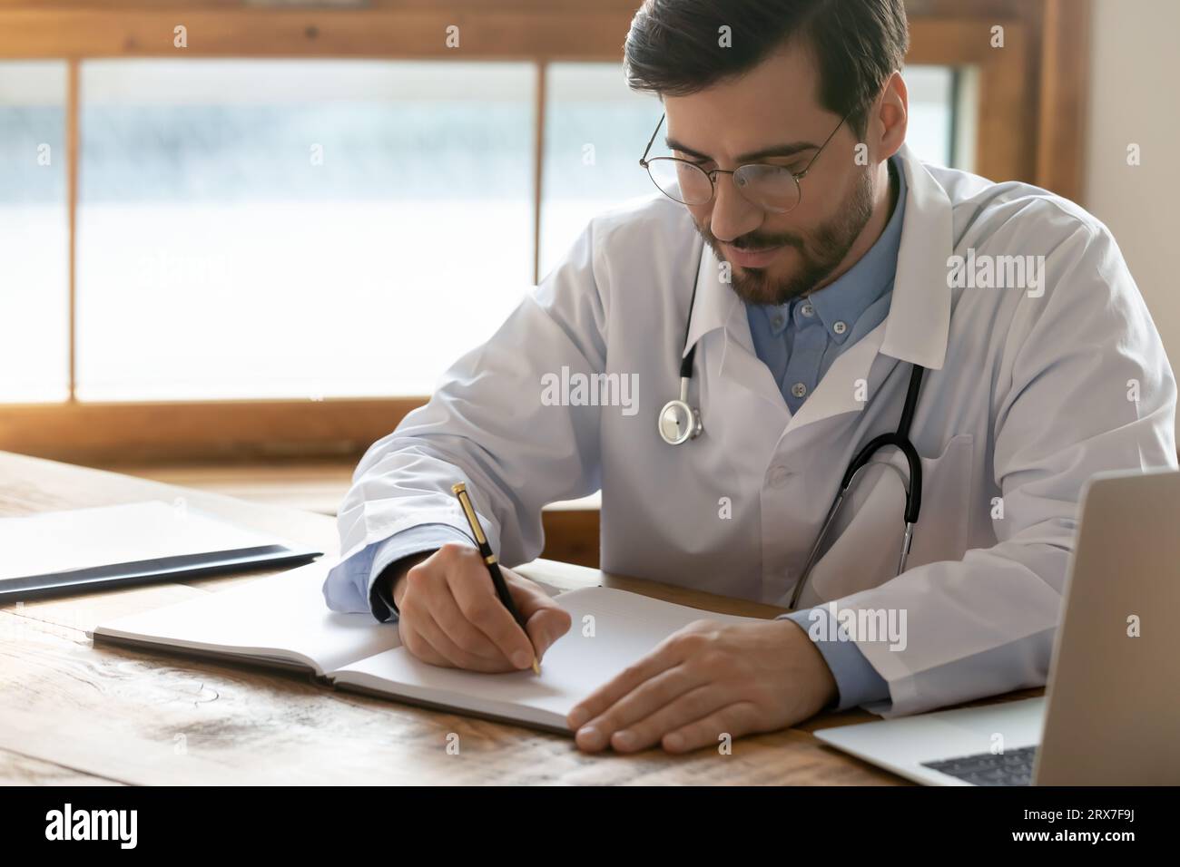 Focused doctor wearing glasses writing illness history in hospital ...