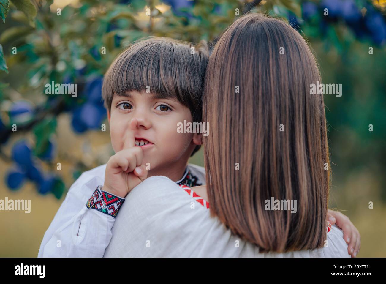 Cute boy showing shhh silence secret gesture on mothers shoulder in ...