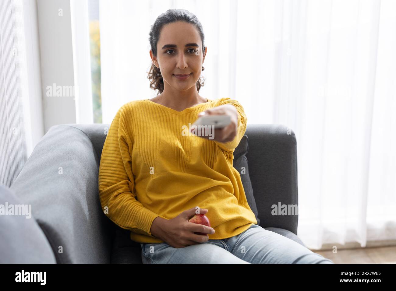 Woman sitting comfortable at home sofa watching tv pointing remote control for changing tv ...