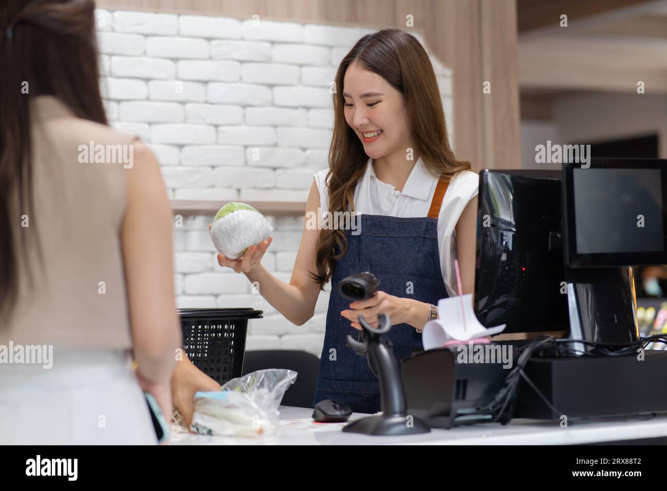 Young smiling Asian female cashier at the supermarket cashier using ...