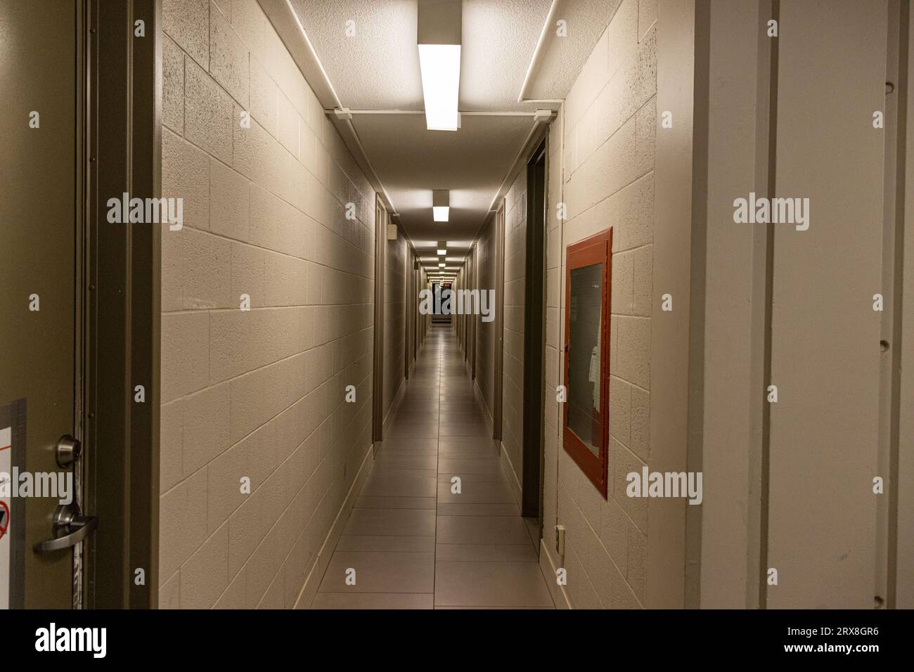A long, narrow hallway with closed gray doors and a red fire ...
