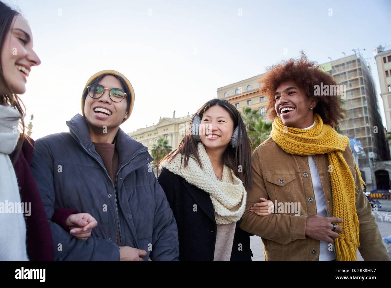 Multiracial colleagues strolling around the city hugging on a winter day. Couples fun outdoors ...