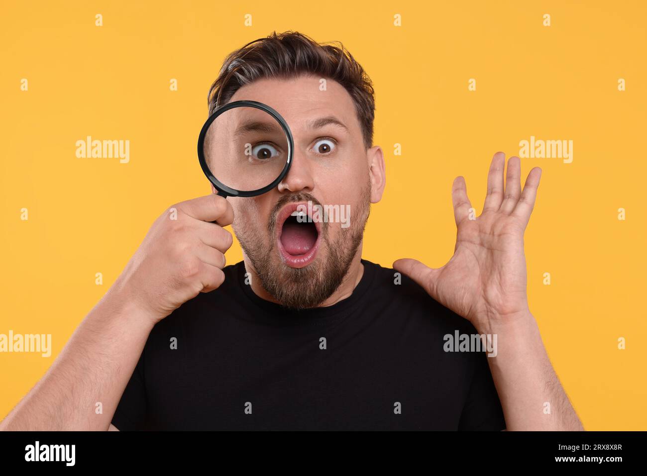 Emotional man looking through magnifier on yellow background Stock ...