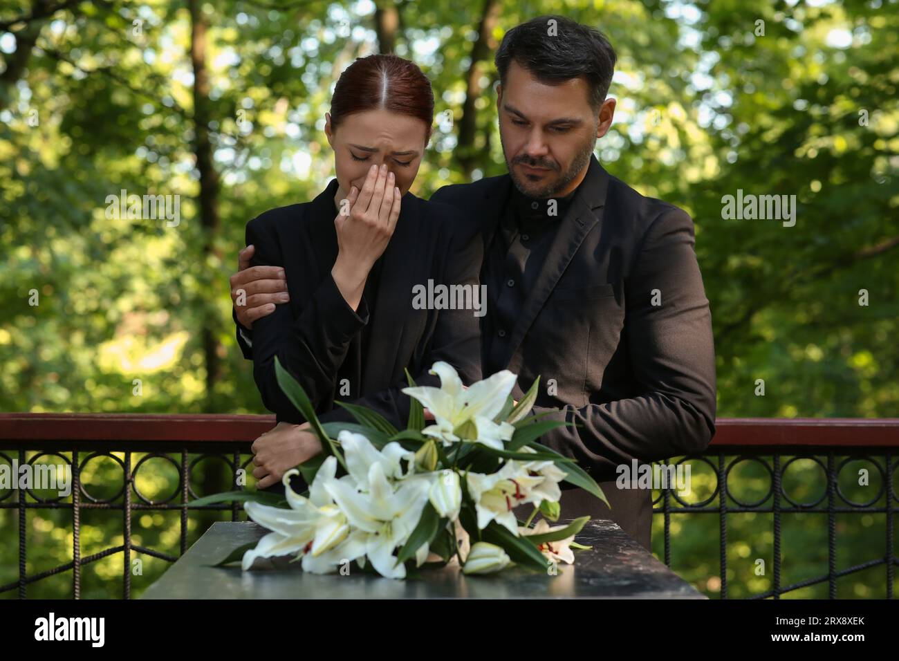 Sad couple mourning near granite tombstone with white lilies at ...