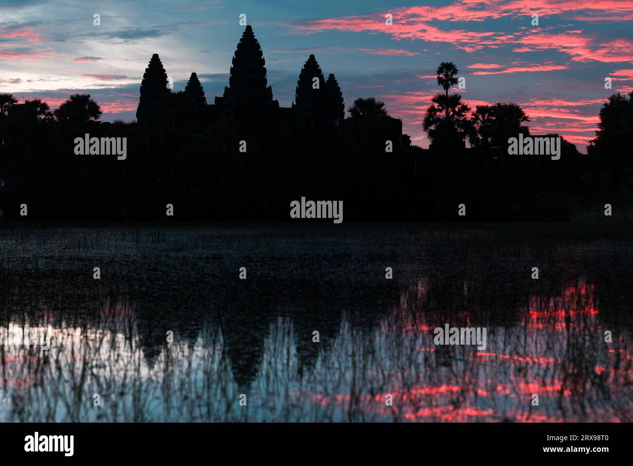 The temples of Angkor Wat in silhouette at sunrise. Reflections are ...