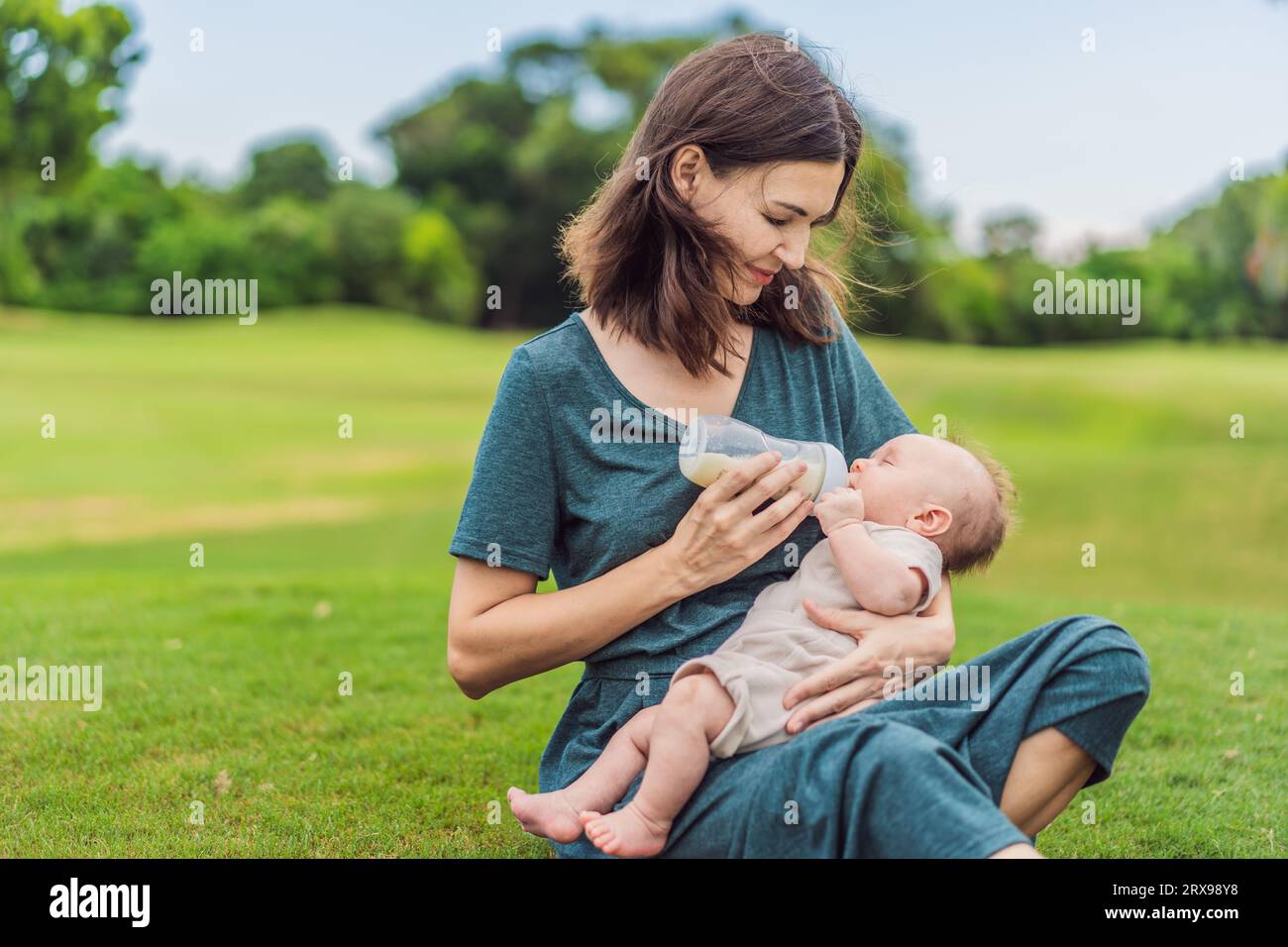 Mother holding and feeding baby from milk bottle in the park. Portrait ...