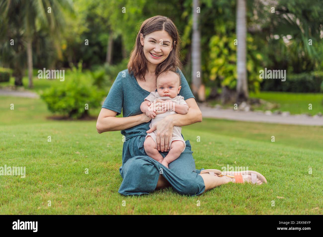 A happy 40-year-old mother cradles her newborn in a sun-drenched park ...