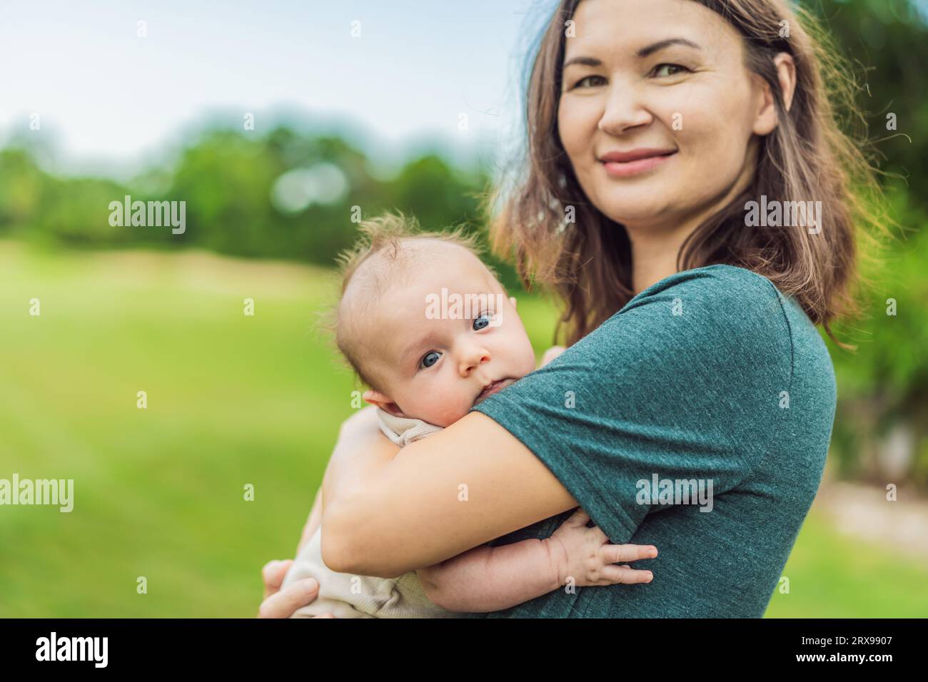 A happy 40-year-old mother cradles her newborn in a sun-drenched park ...