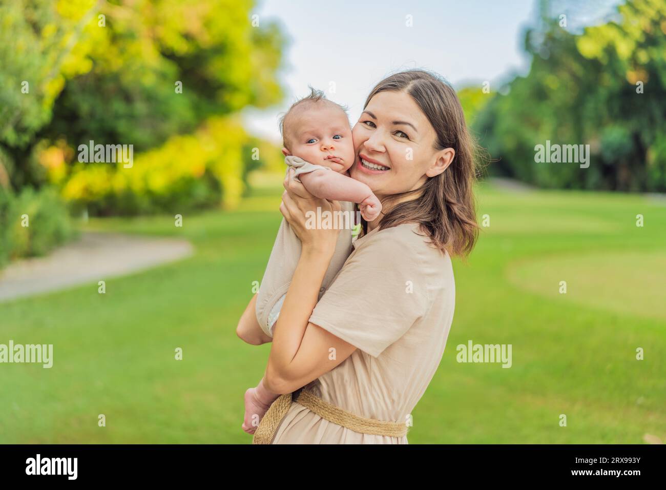 A happy 40-year-old mother cradles her newborn in a sun-drenched park ...