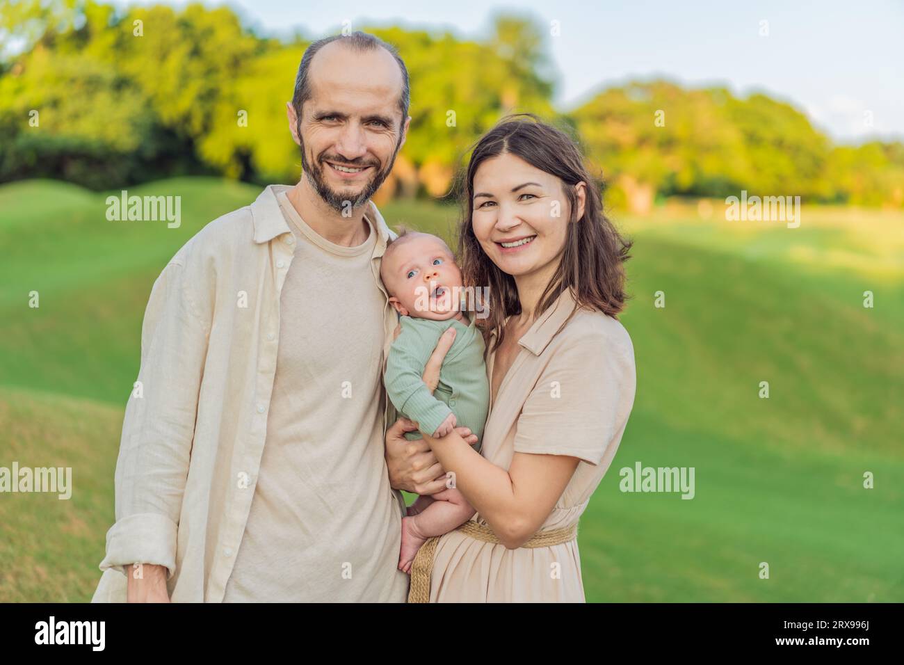 A happy 40-year-old couple cradles their newborn in a sun-drenched park ...