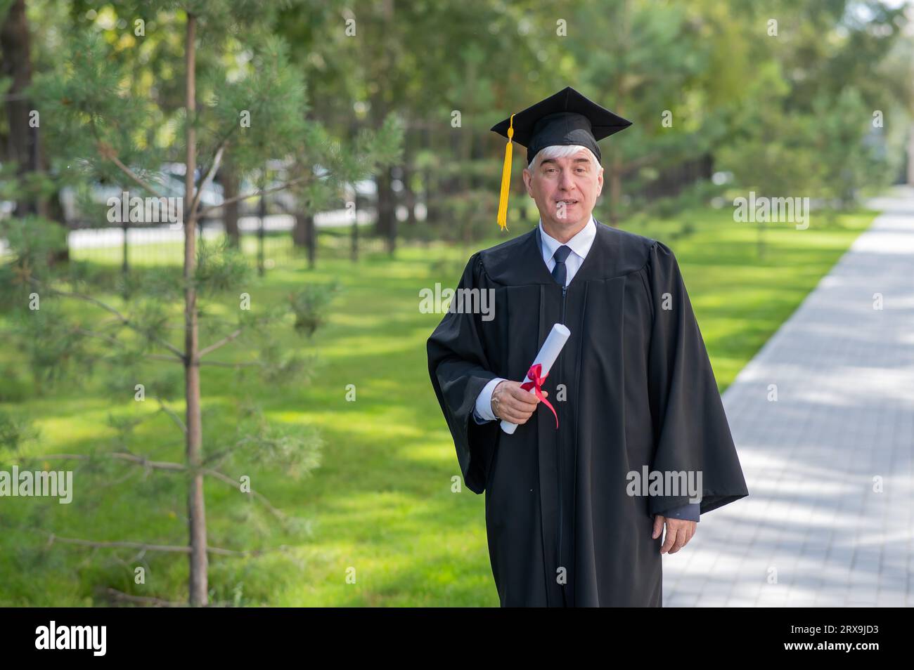 Serious old man in graduation gown holding diploma outdoors Stock Photo ...
