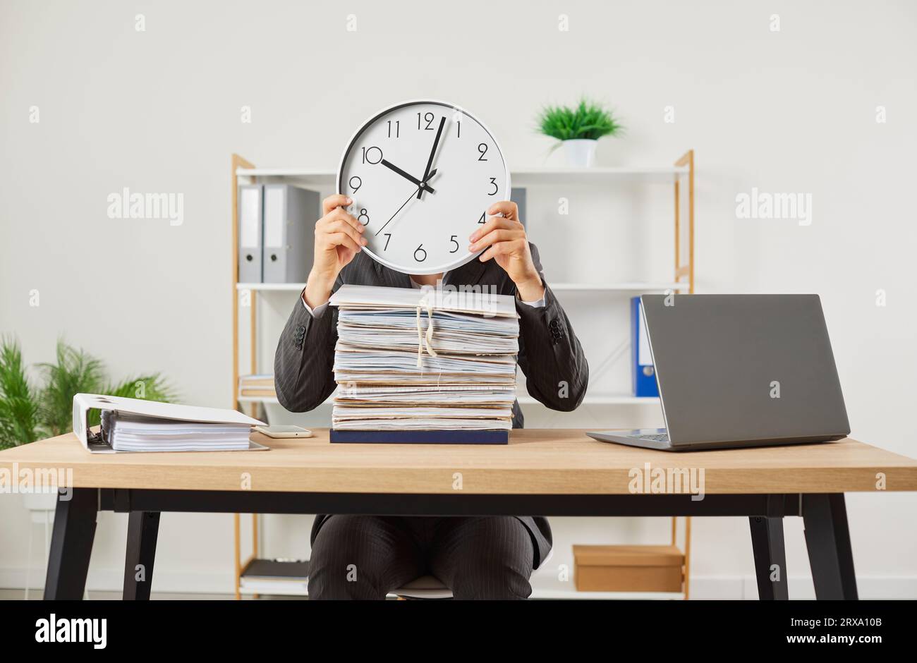 Funny worker employee hiding head behind the clock at workplace in ...