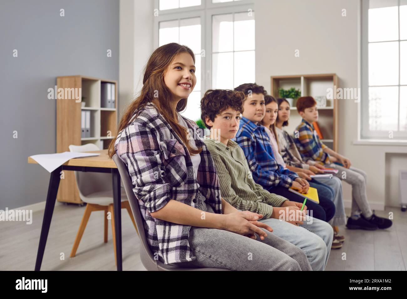 Smiling elementary school children sitting on chairs in row in ...