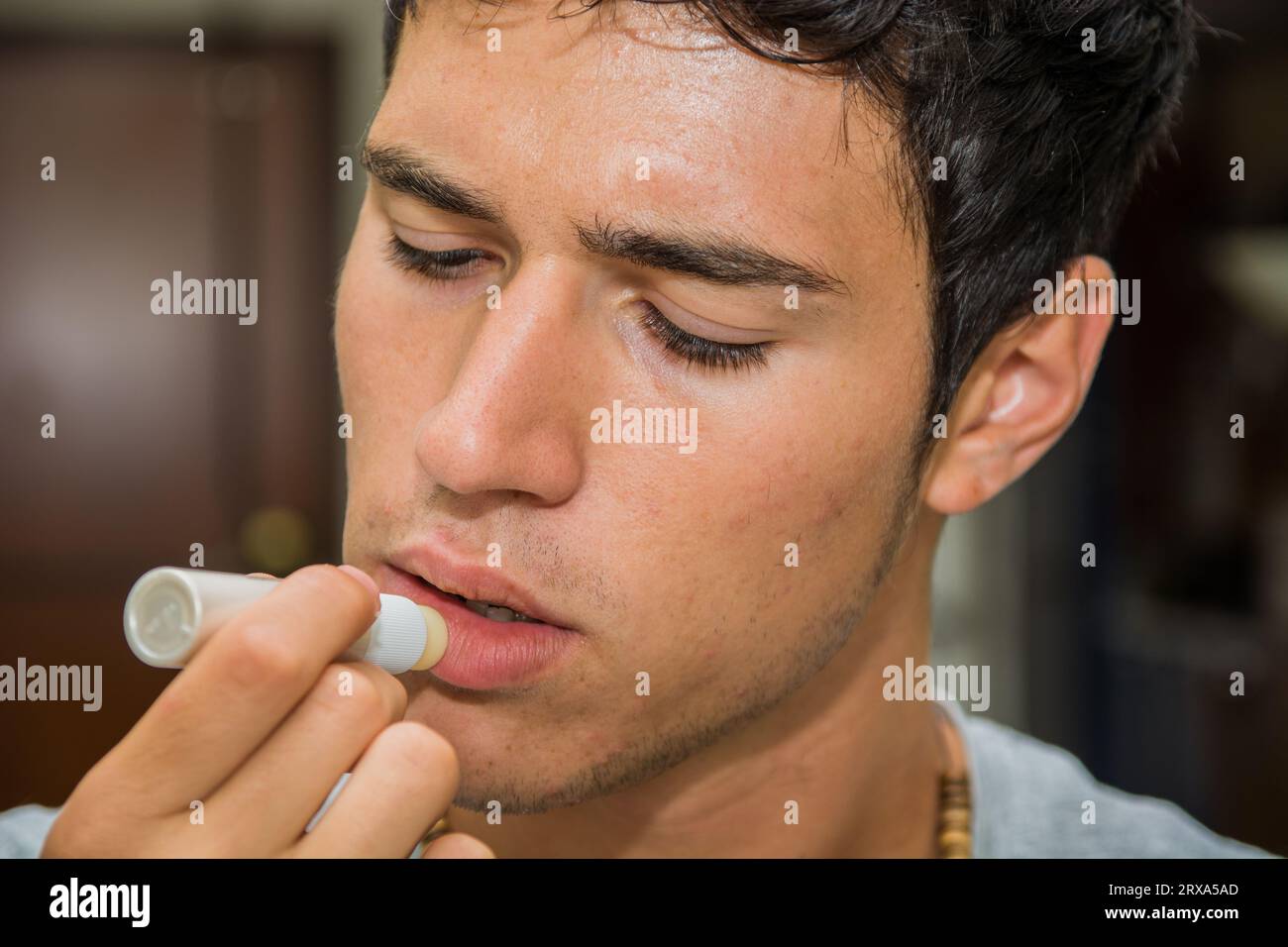 A man with a necklace on putting a li balm on his mouth. Photo of a ...