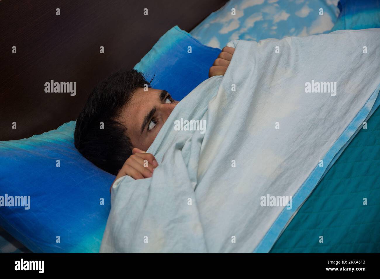 A person laying in a bed with a blue pillow, with his eyes wide open ...