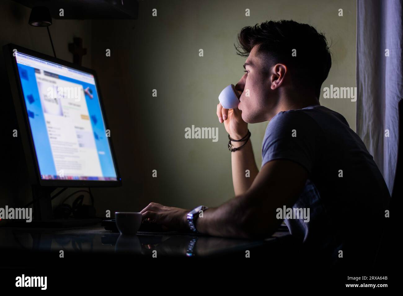 A man sitting in front of a computer screen, drinking an espresso ...