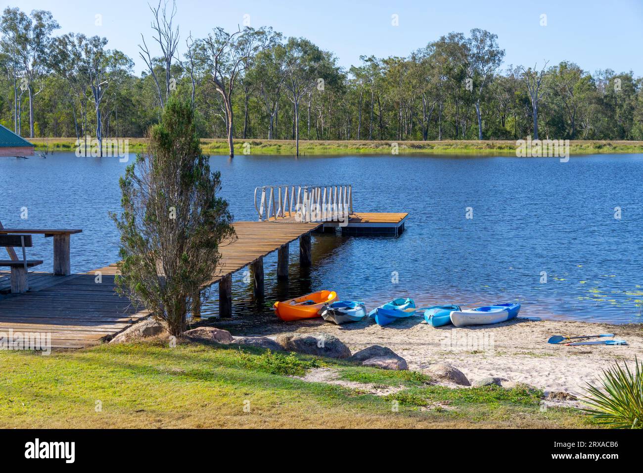 Kayaks on sandy beach of freshwater dam by jetty with pontoon on sunny ...