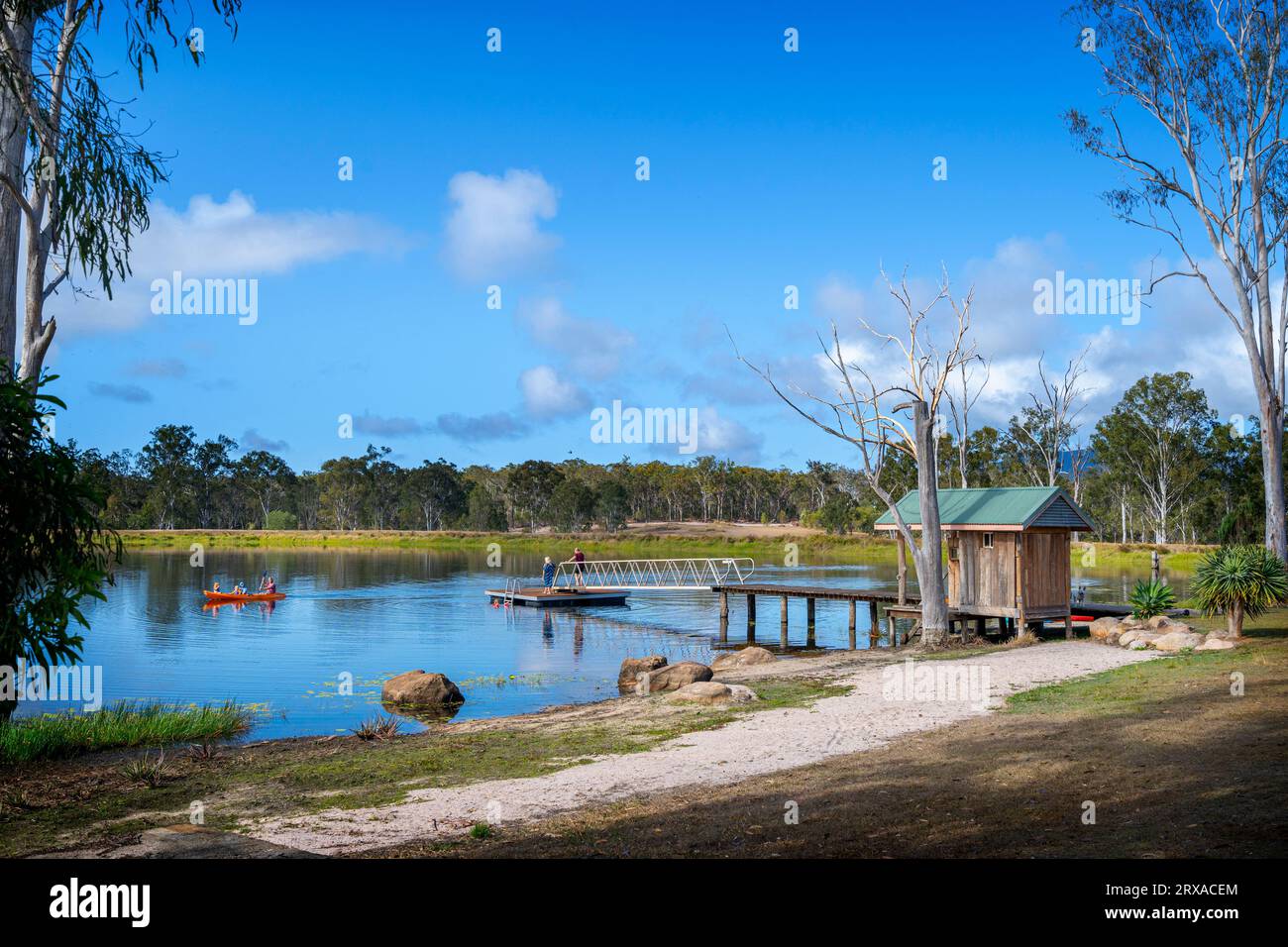 Kayaks on sandy beach of freshwater dam by jetty with pontoon on sunny ...
