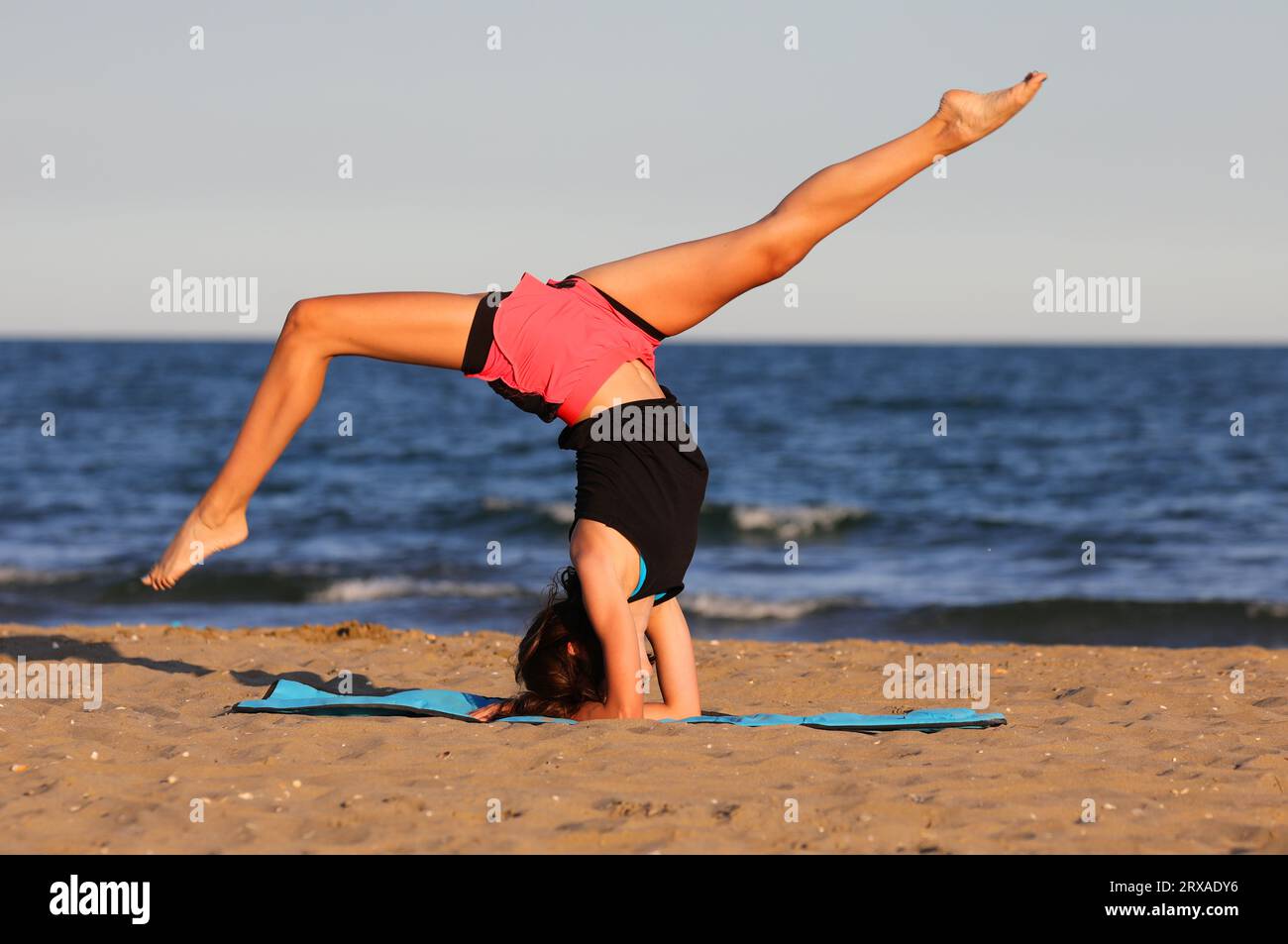 athletic slender girl by the sea does gymnastic training with head down ...