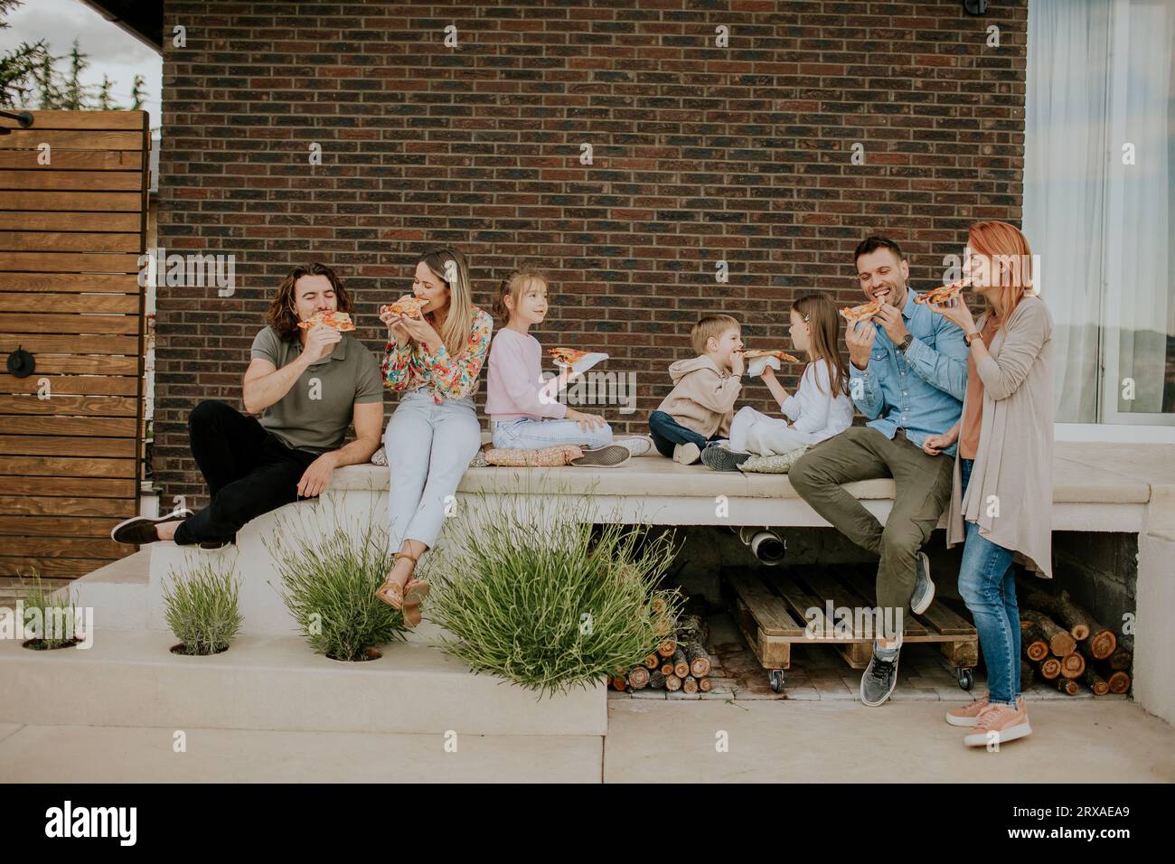 Happy group of young people and kids eating pizza in the house backyard ...