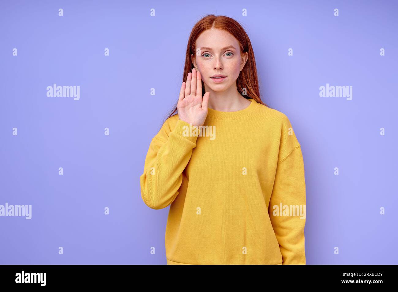 Young deaf mute red-haired woman using sign language on blue background ...