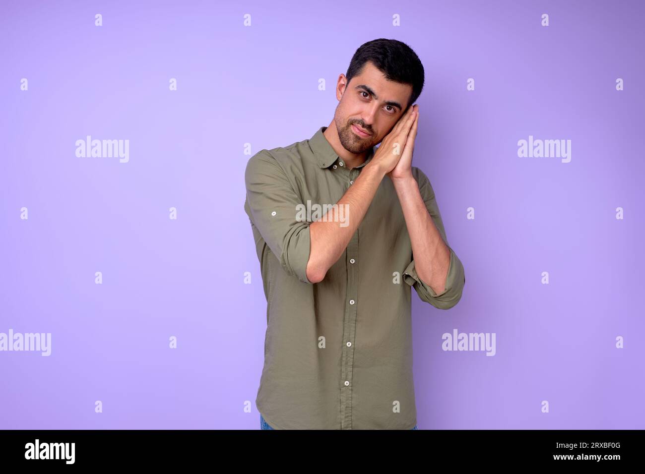 serious handsome man showing sleeping gesture, lying on folded hands ...