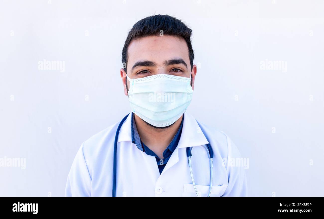 Young male wearing mask and doctor coat while holding stethoscope on ...