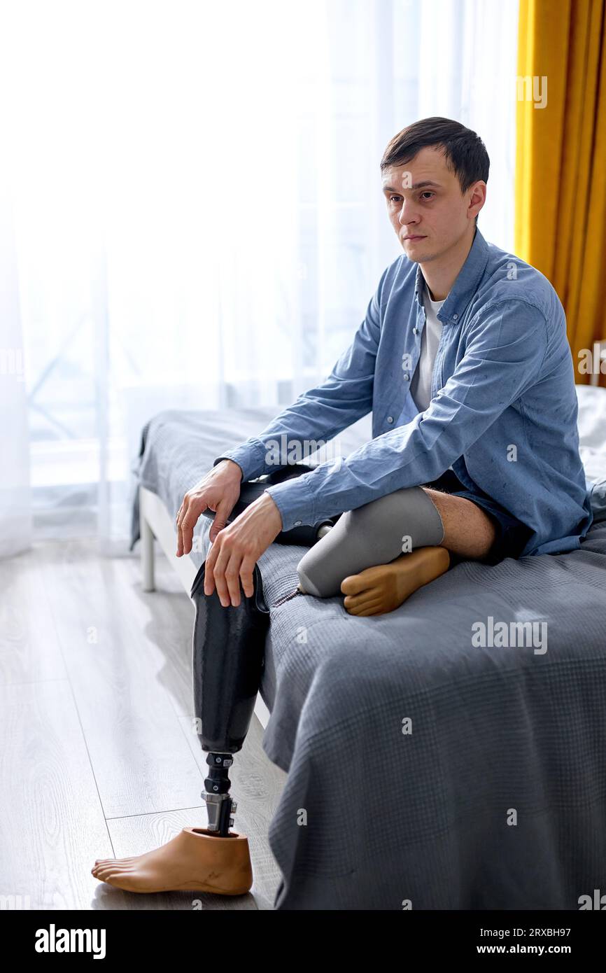 young man leg amputee wearing or changing prostheses at home sitting on ...