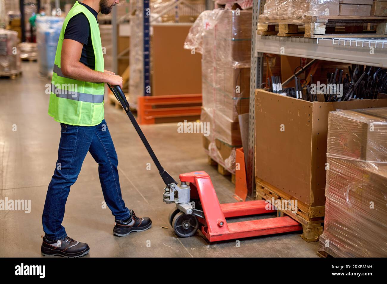 worker in a warehouse uses hand pallet stacker to transport pallets ...