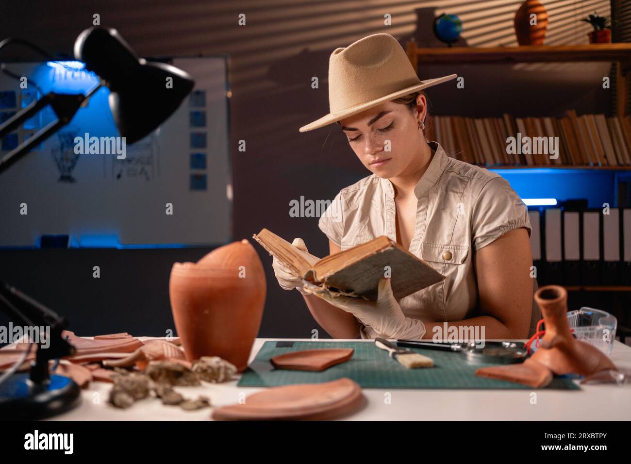 Archeologist working late night in office reading old book about ...