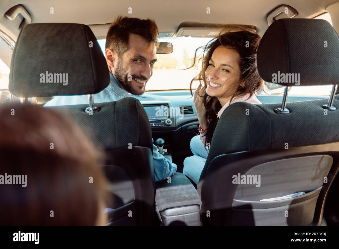Back view of happy family riding car, mother and father turning back to ...