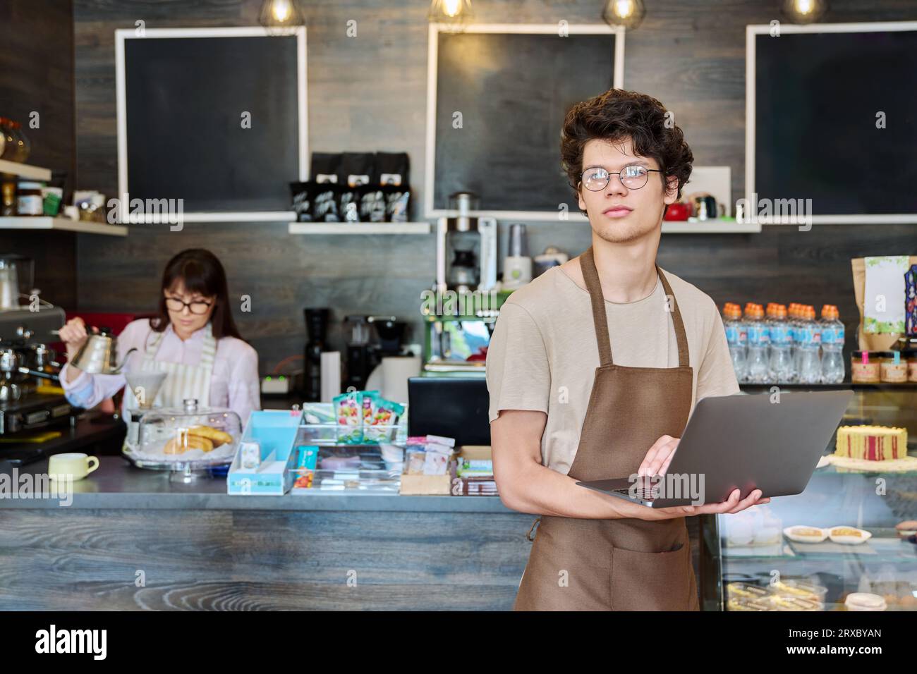 Young guy in an apron with laptop in his hands inside coffee shop ...