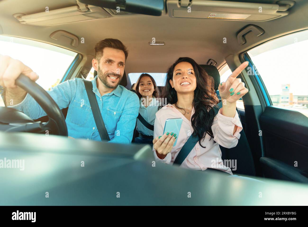 Happy family of three driving automobile, woman using cellphone gps ...