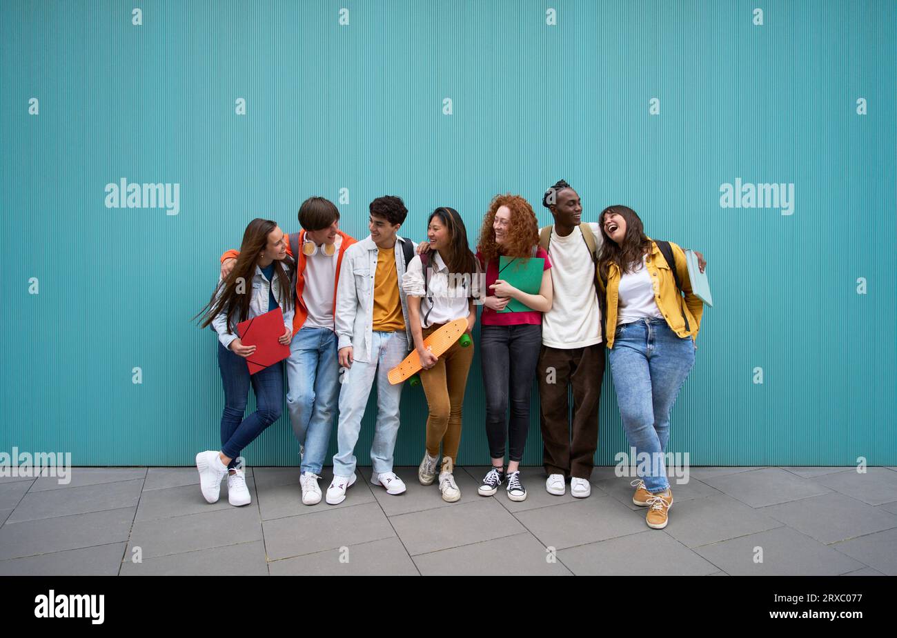 Large group of cheerful young people leaning against blue wall ...