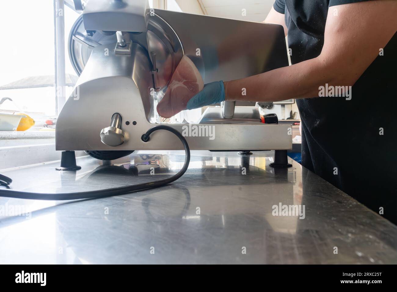A male employee, wearing blue gloves, skilfully operated a slicing ...
